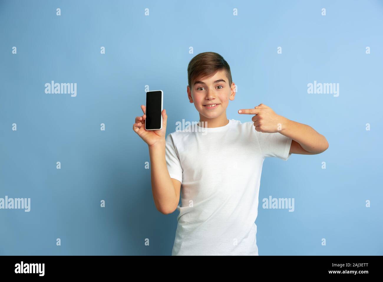 Showing blank phone's screen. Caucasian boy portrait isolated on blue ...