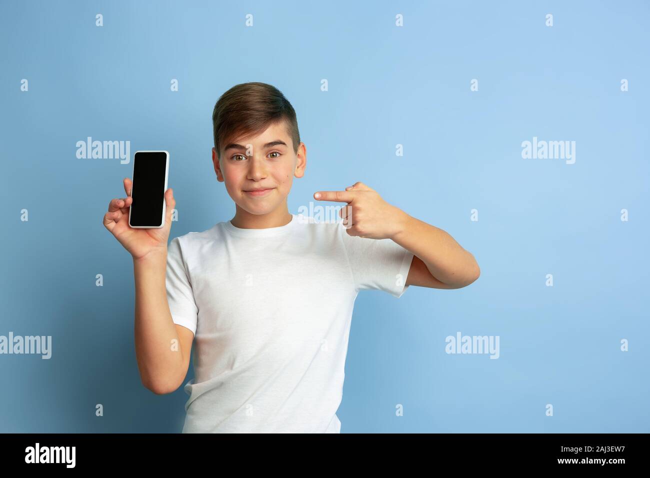 Showing blank phone's screen. Caucasian boy portrait isolated on blue ...