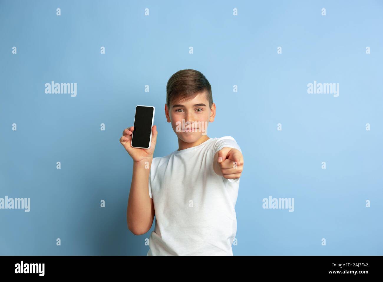 Showing blank phone's screen. Caucasian boy portrait isolated on blue ...