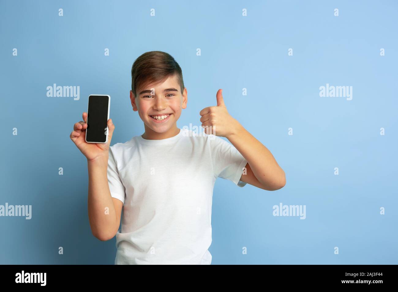 Showing blank phone's screen. Caucasian boy portrait isolated on blue ...