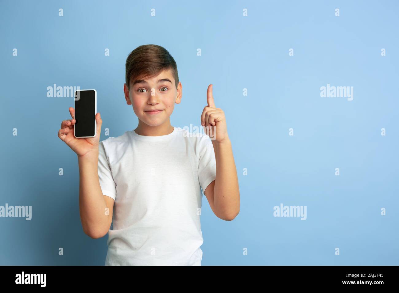 Showing blank phone's screen. Caucasian boy portrait isolated on blue ...