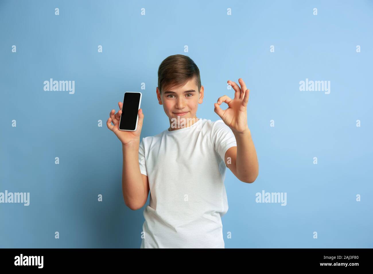 Showing blank phone's screen. Caucasian boy portrait isolated on blue ...
