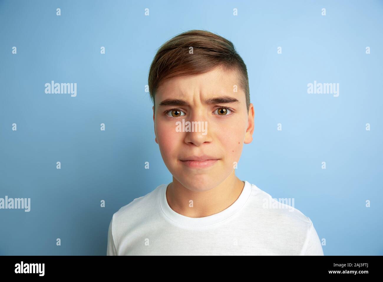 Angry, sad. Close up. Caucasian boy portrait isolated on blue studio ...