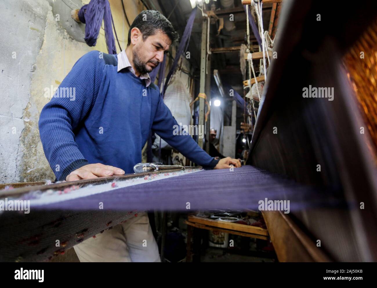 A Palestinian worker weaves carpets on a traditional wooden loom at a ...