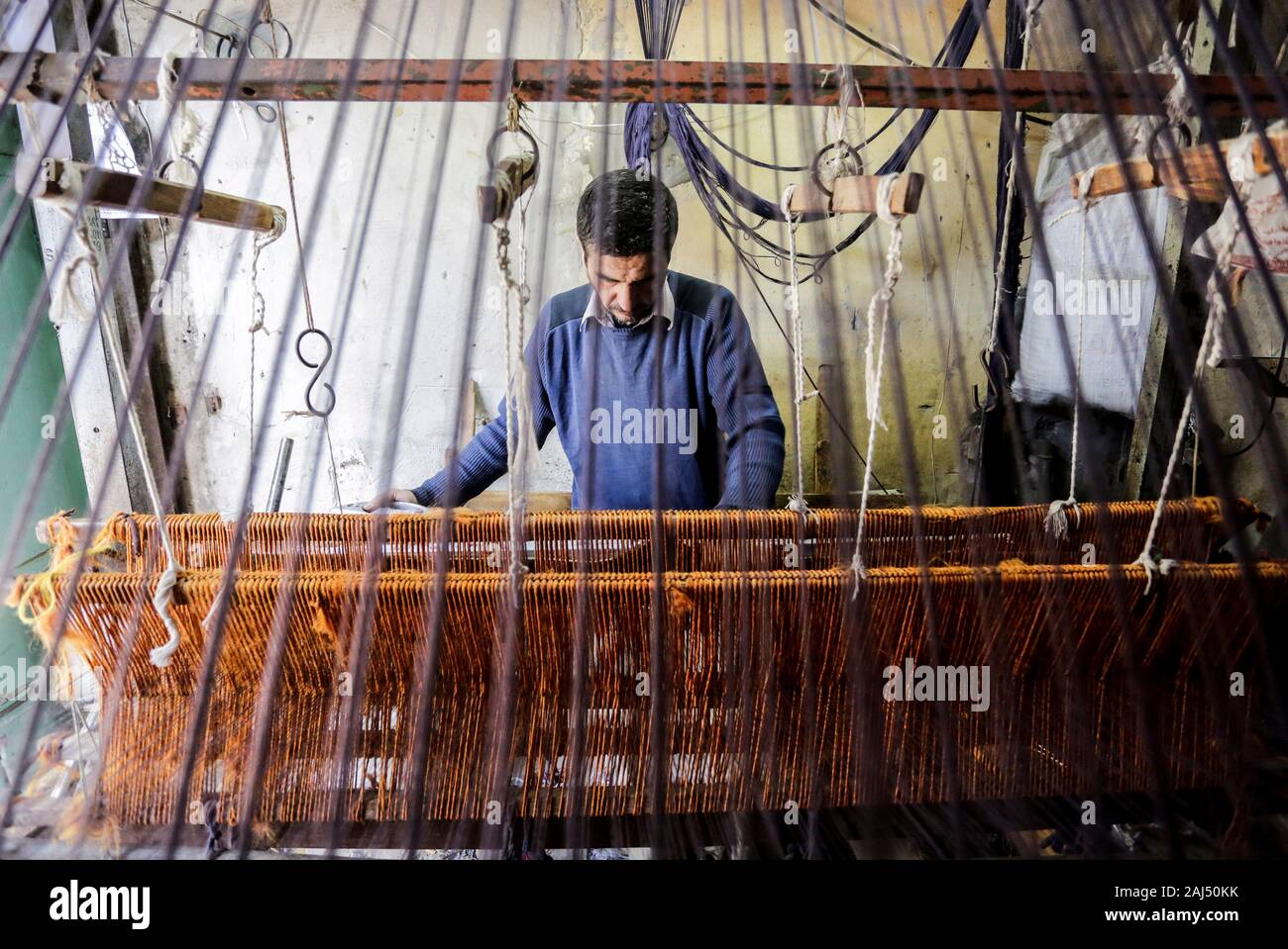A Palestinian worker weaves carpets on a traditional wooden loom at a ...