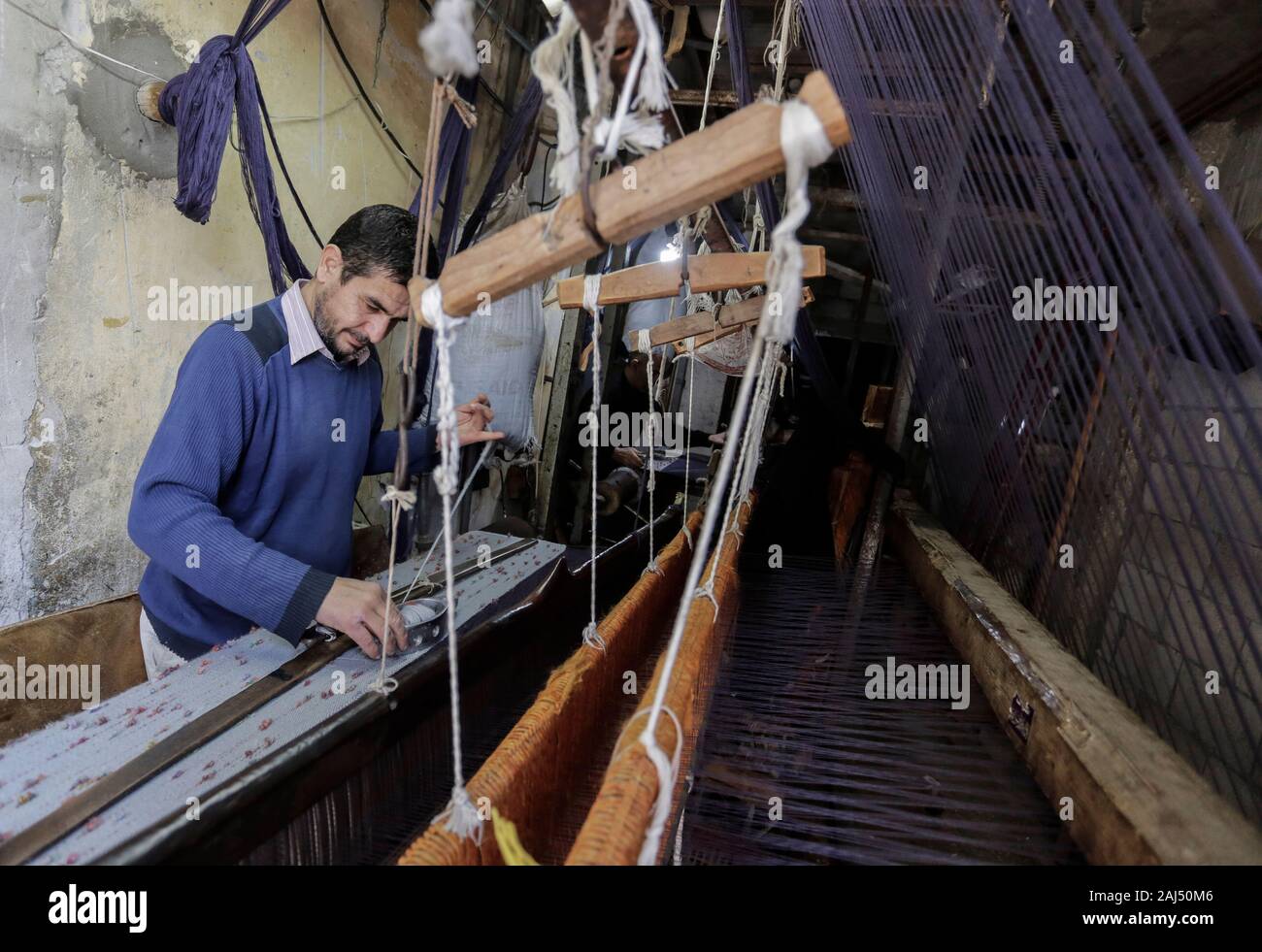 A Palestinian worker weaves carpets on a traditional wooden loom at a ...