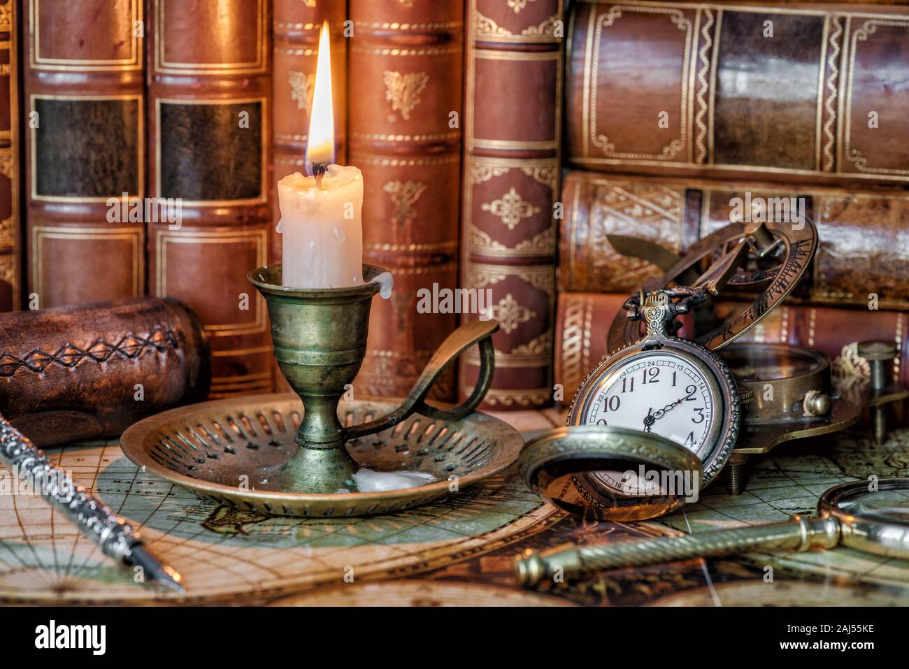 Vintage pocket watch and burning candle in an old candlestick are on ...