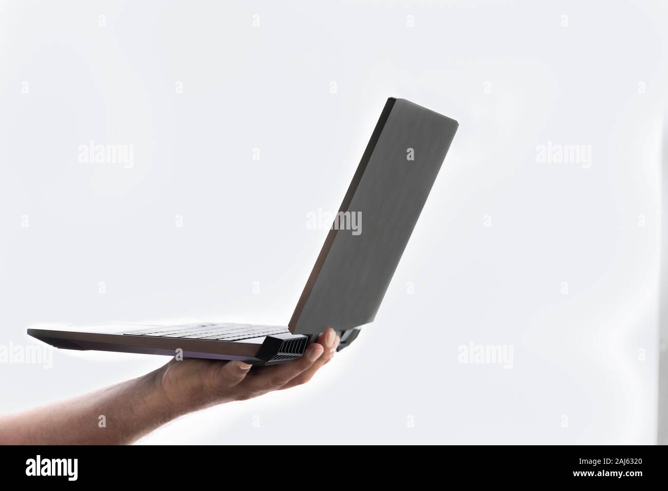 Close-up of a laptop being held by a hand on a light background ...