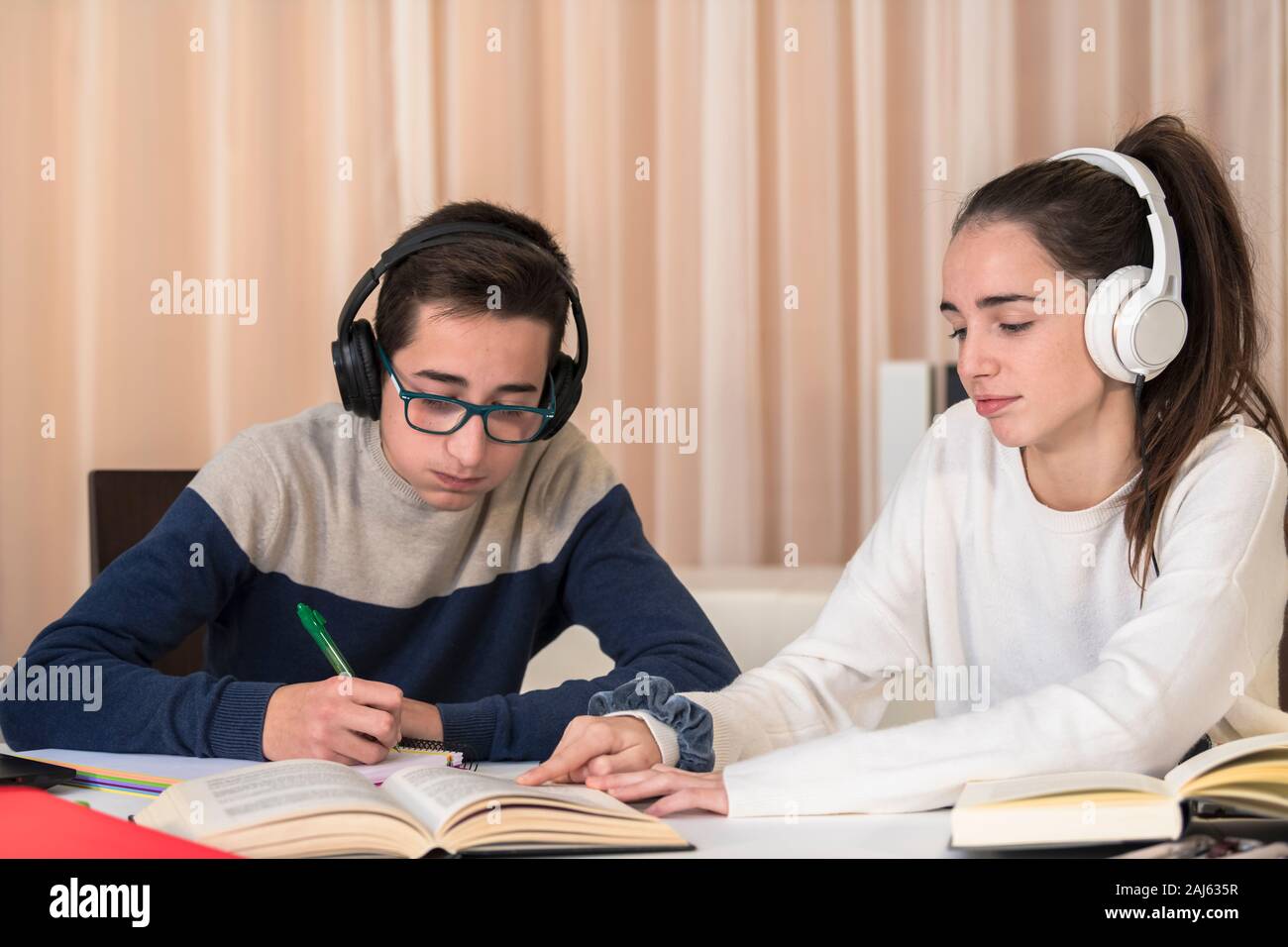 A couple of tired looking teenagers read a book and take notes while ...