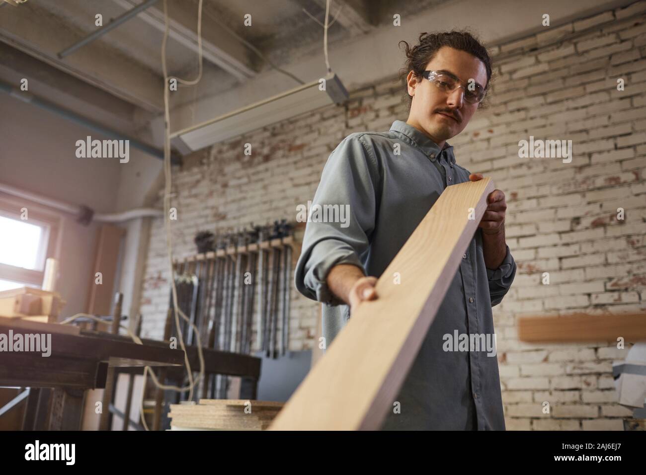 Young serious worker examining wooden detail while working at carpentry ...