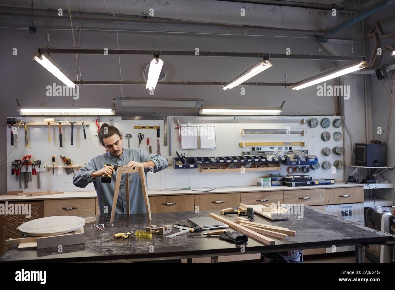 Carpenter standing near the workplace with wooden chair on it and using ...