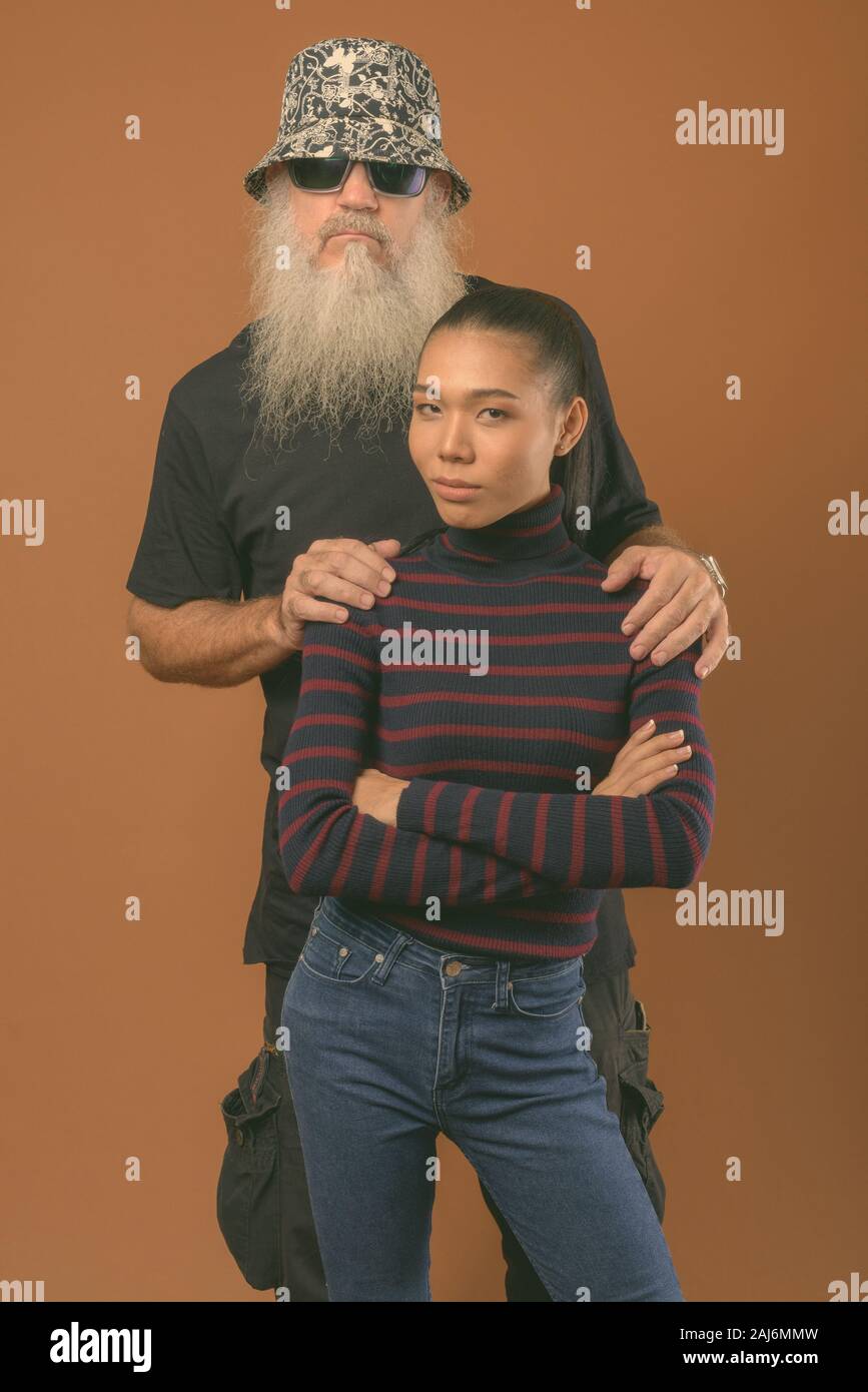Studio shot of mature bearded bald man and young beautiful Asian ...