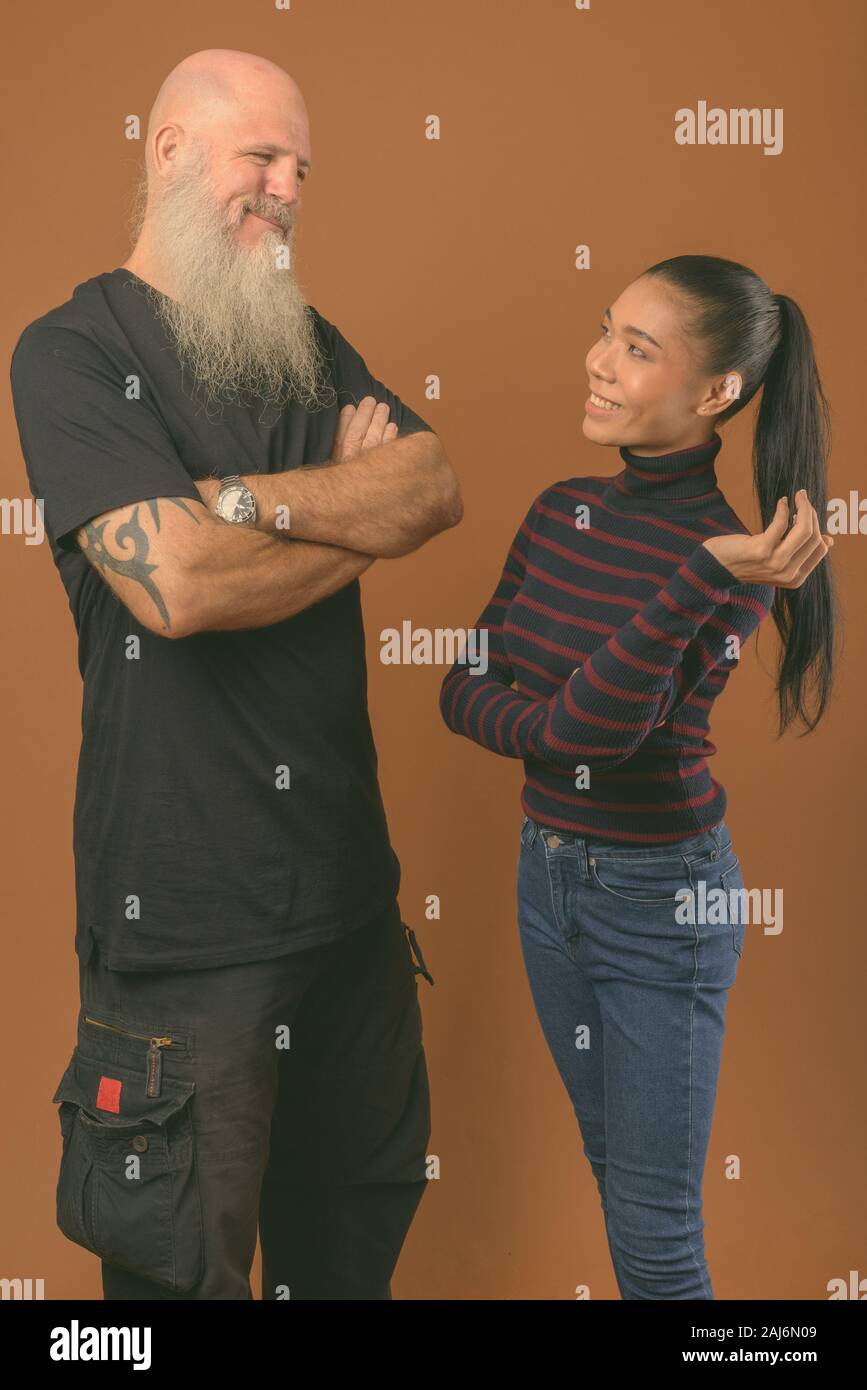 Studio shot of mature bearded bald man and young beautiful Asian ...