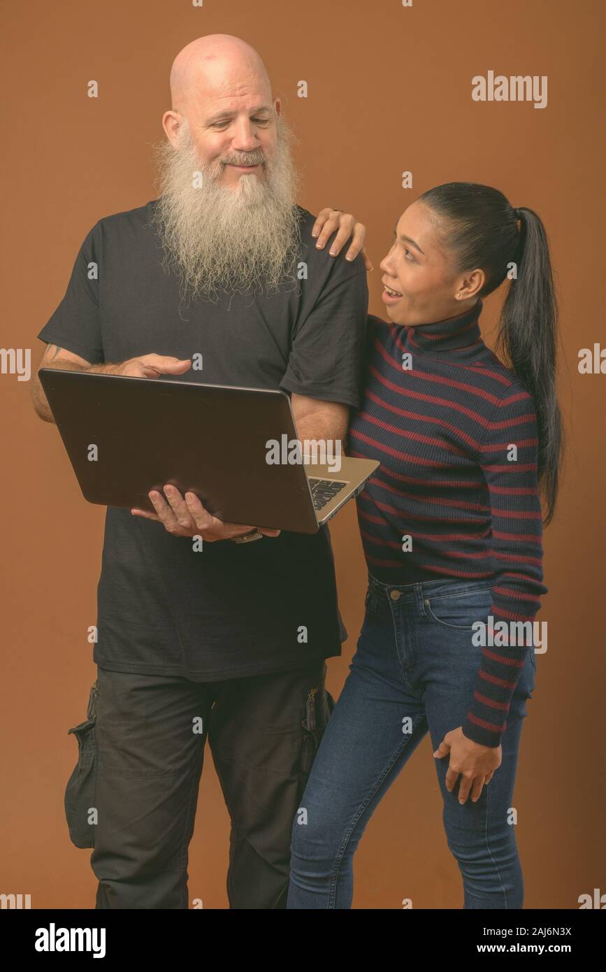 Studio shot of mature bearded bald man and young beautiful Asian ...