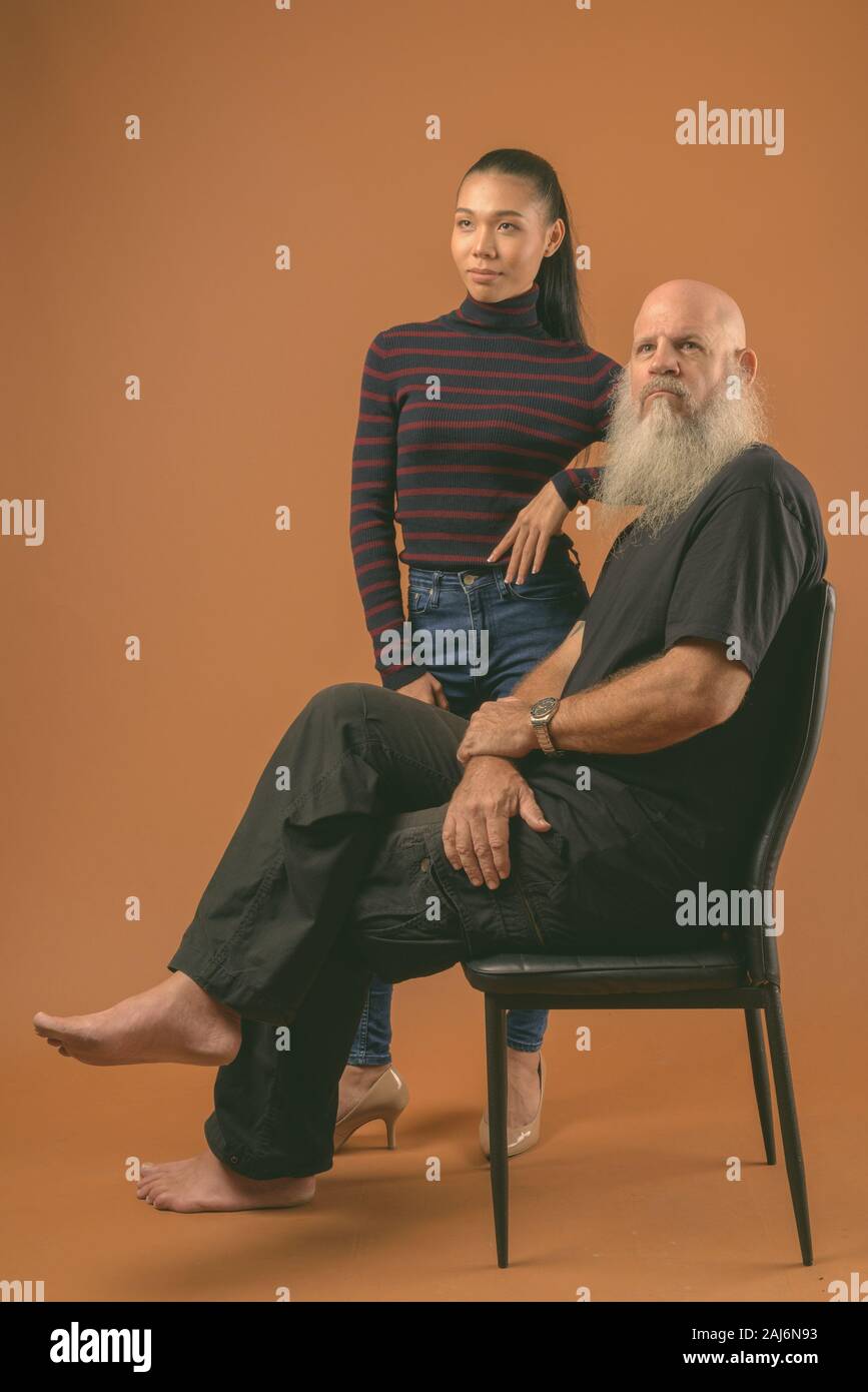 Studio shot of mature bearded bald man and young beautiful Asian ...