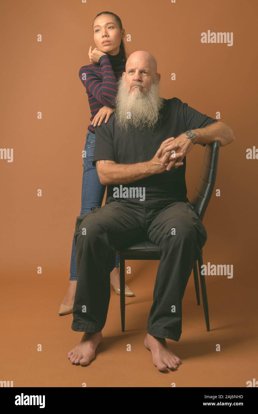 Studio shot of mature bearded bald man and young beautiful Asian ...