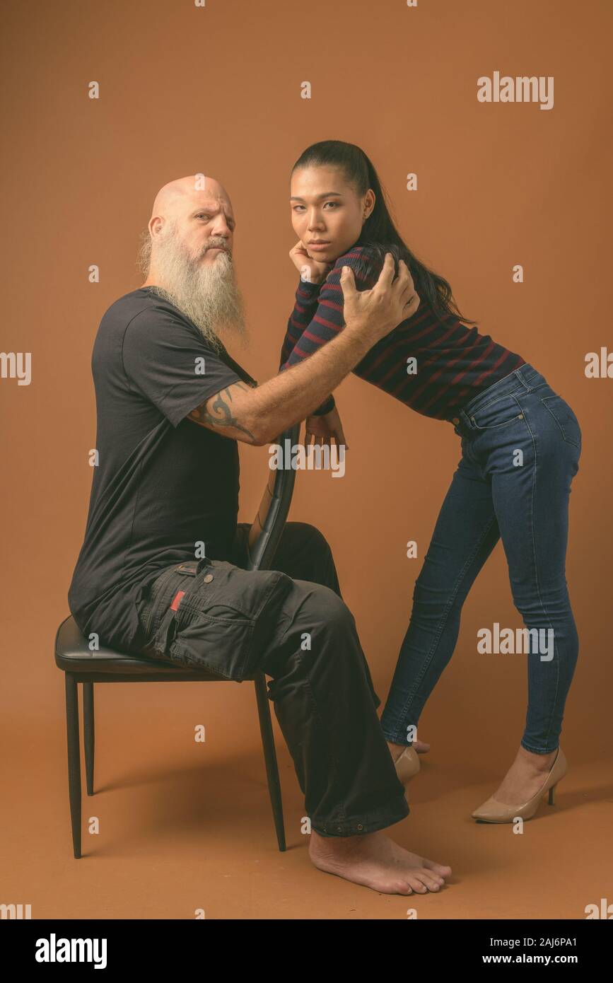 Studio shot of mature bearded bald man and young beautiful Asian ...