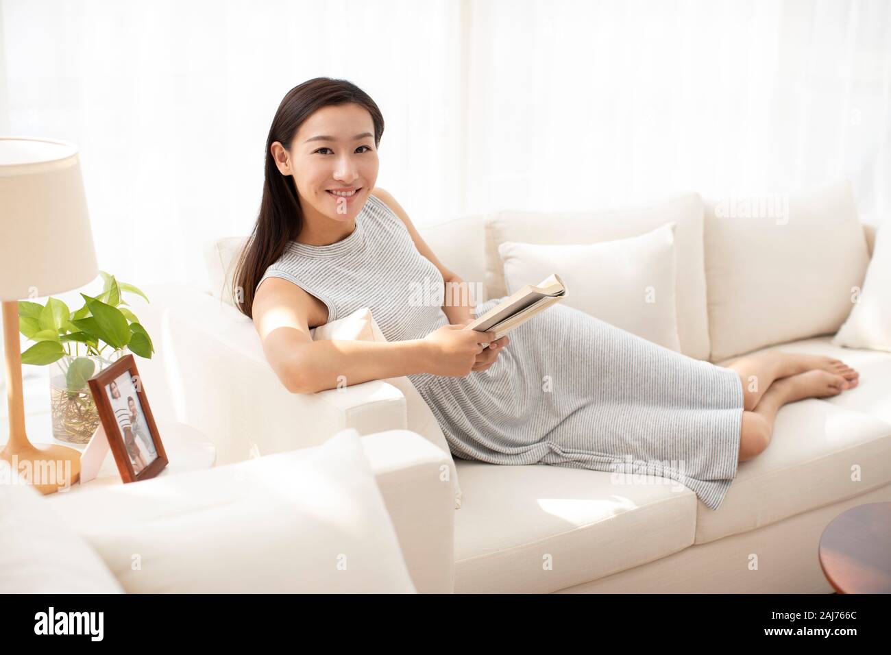 Young Chinese woman reading book on sofa Stock Photo - Alamy