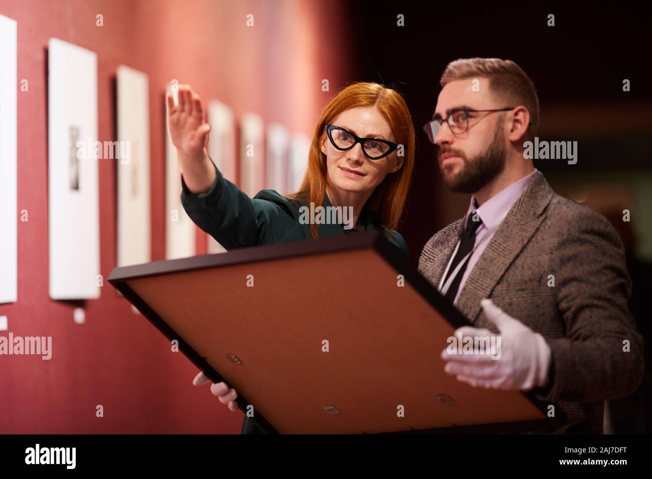 Young red haired art manager showing the place for new painting to her ...