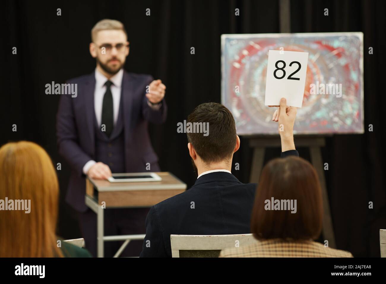 Rear view of young man raising his sign with number he is going to buy ...