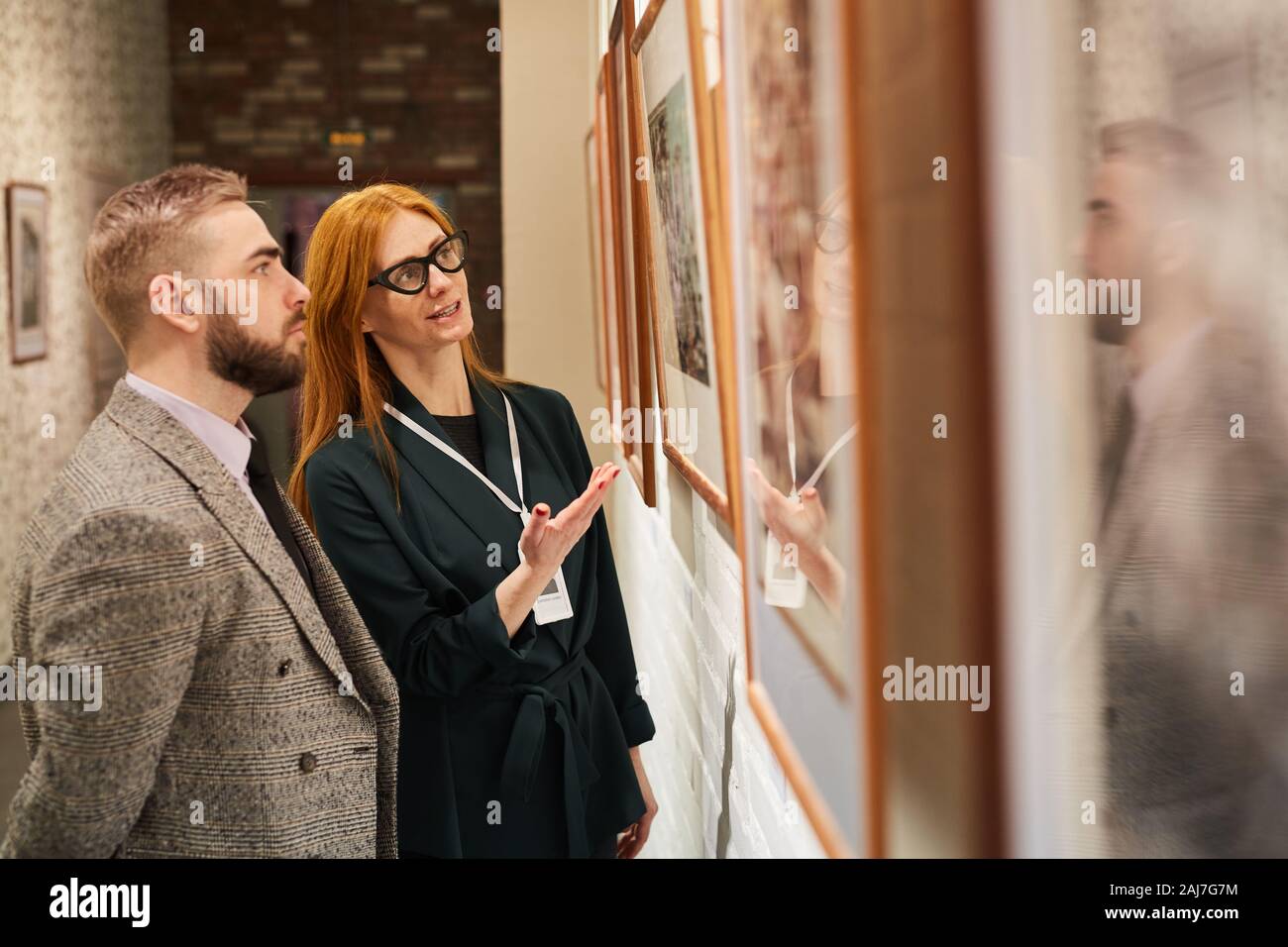 Young art manager pointing at painting and telling about it to young ...