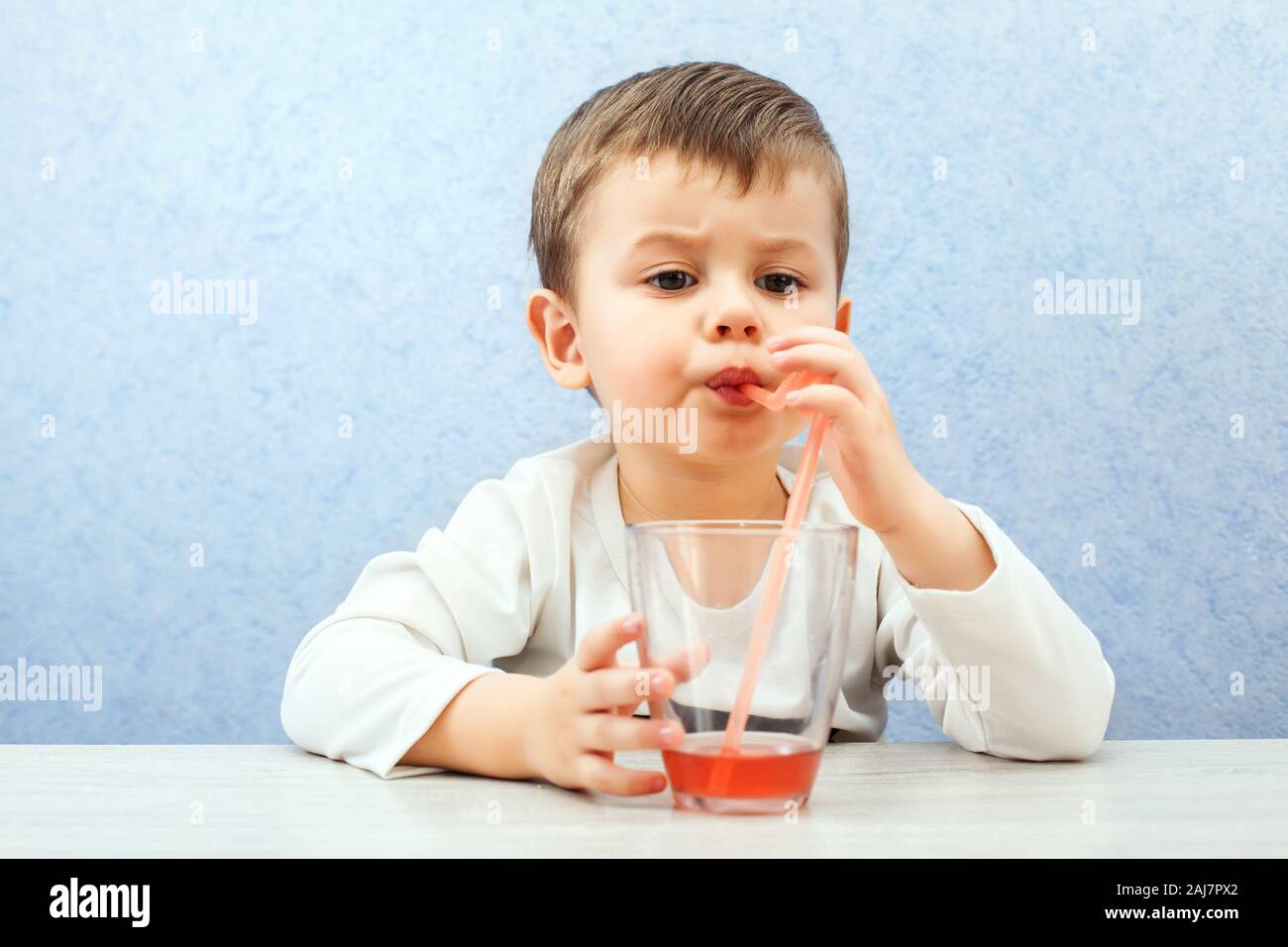 Cute little boy drinking juice on light blue background. Lovely kid ...