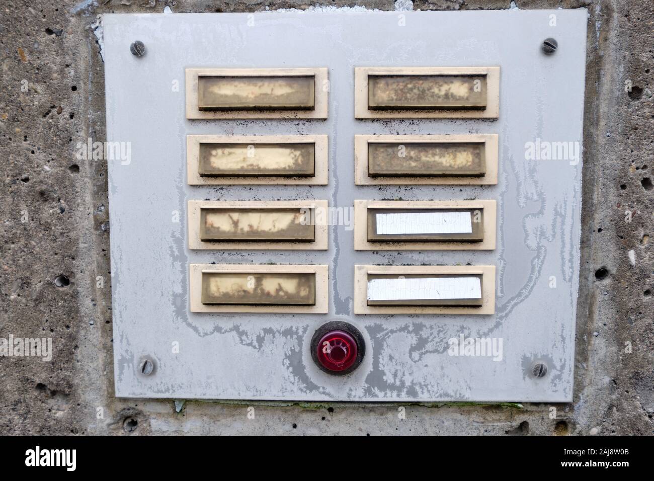 Old and weathered metal doorbell panel with unreadable names with a red ...