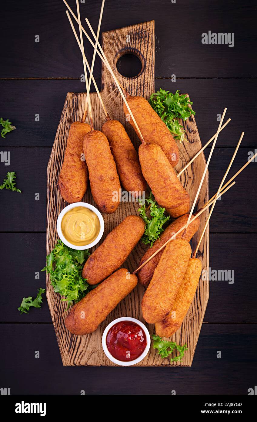 Traditional American corn dogs with mustard and ketchup on wooden board ...