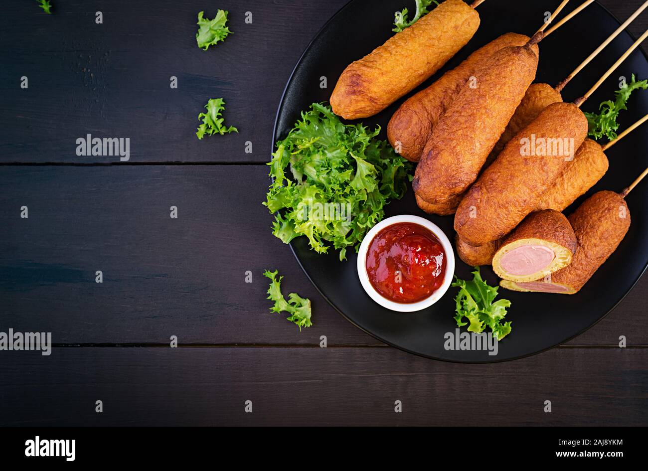 Traditional American corn dogs with mustard and ketchup on black plate ...