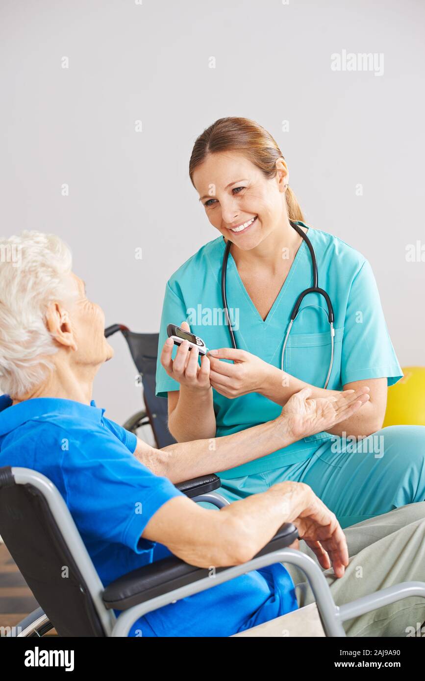 Smiling nurse makes a test for blood sugar in old woman in nursing home ...