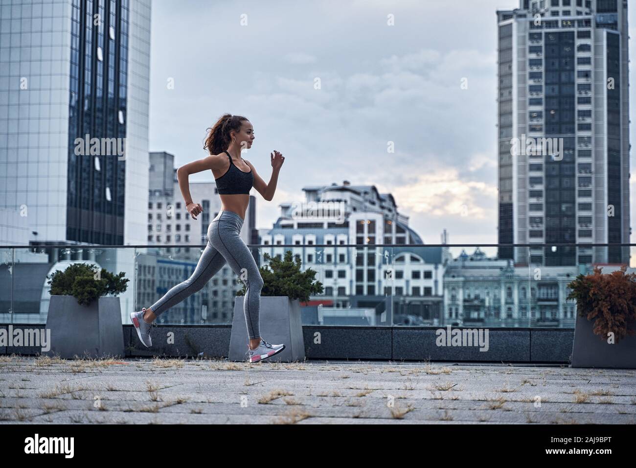 Young athletic woman running in the modern city with skyscrapers on the ...