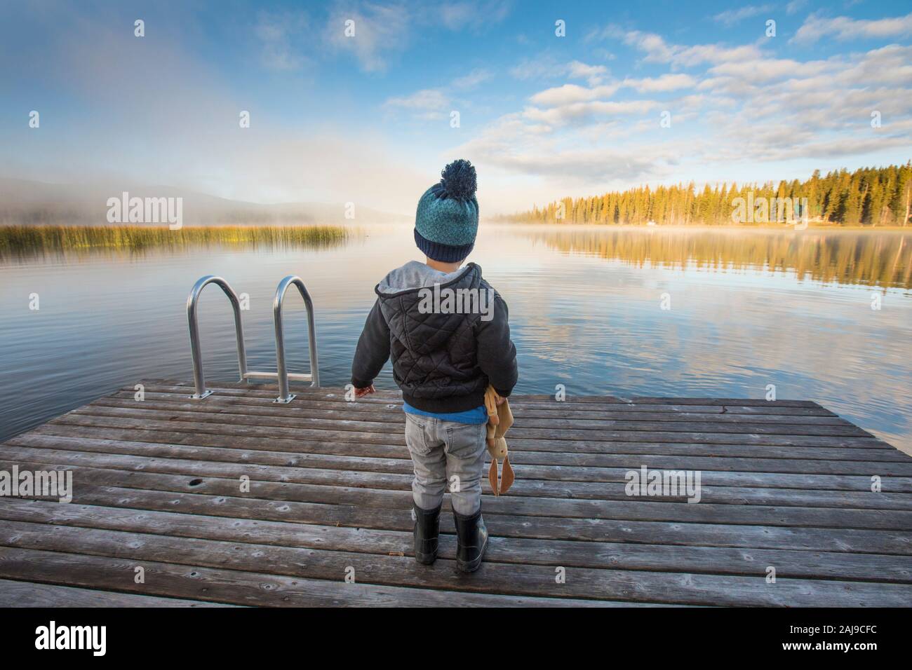 Young boy standing on dock looking out over calm lake Stock Photo - Alamy