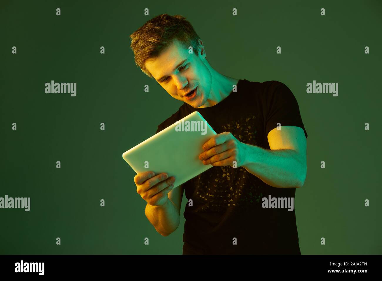 Playing with tablet. Caucasian man's portrait isolated on green studio ...