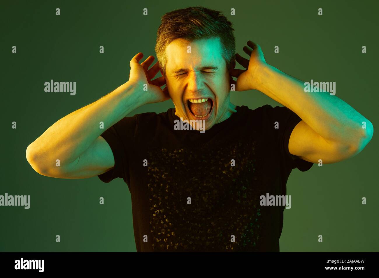 Closes ears, screaming. Caucasian man's portrait isolated on green ...
