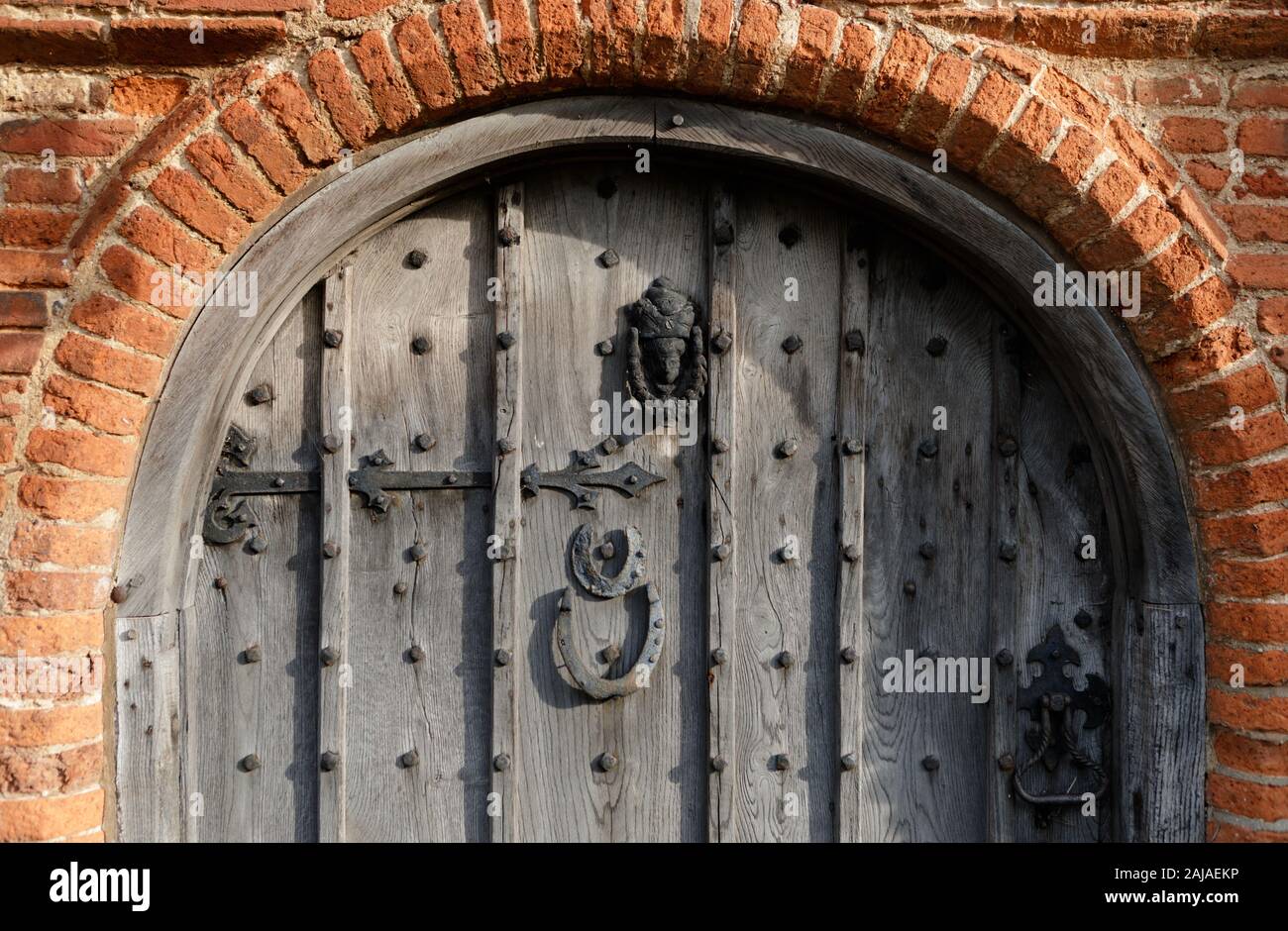 Tudor red brick arch framing a heavy wooden door with lucky horse shoes ...
