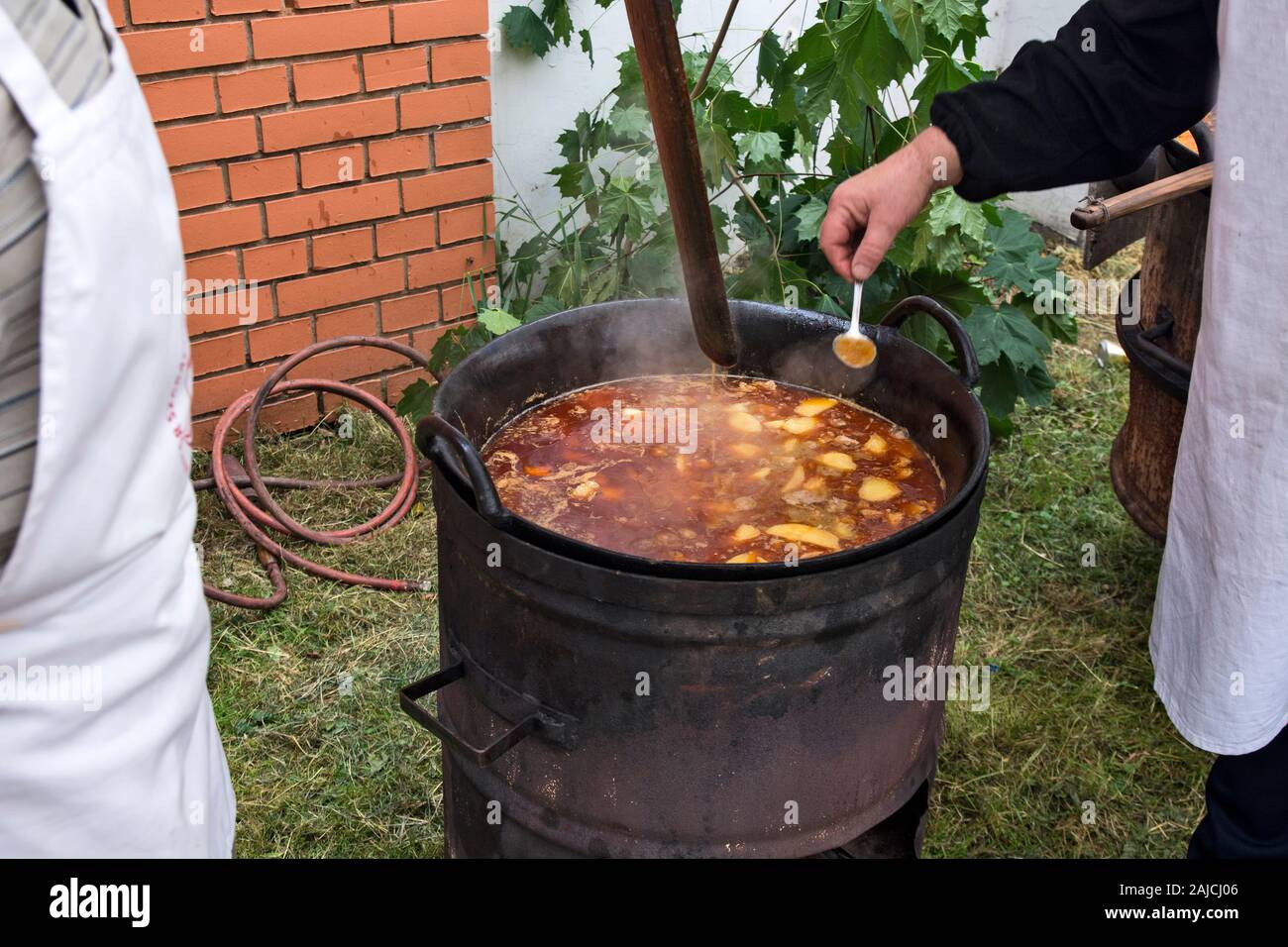 Traditional stew cooking in a large metal outdoor cauldron. Tasting of ...