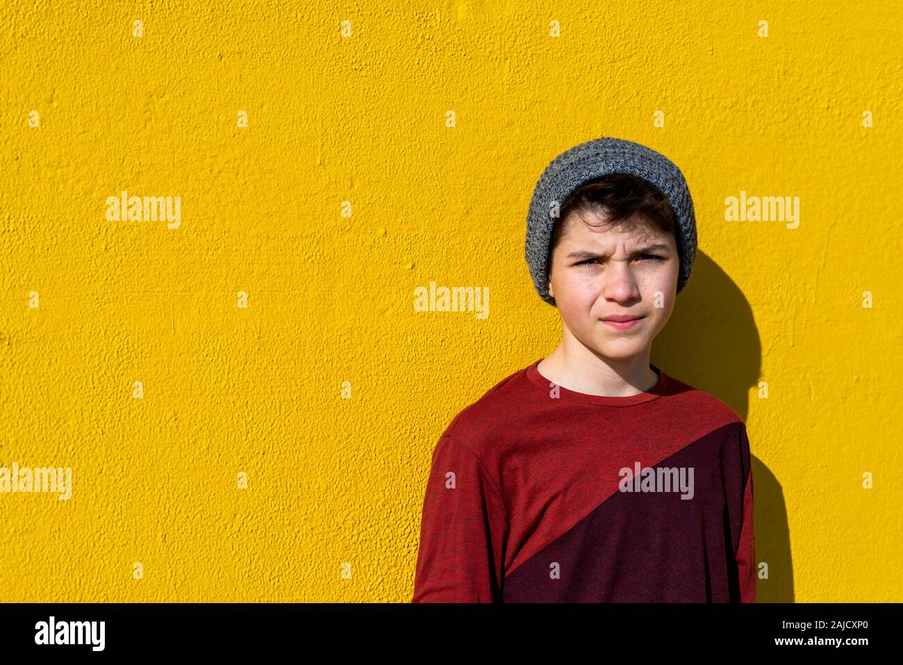 Teen with wool cap leaning against a yellow wall while looking camera ...