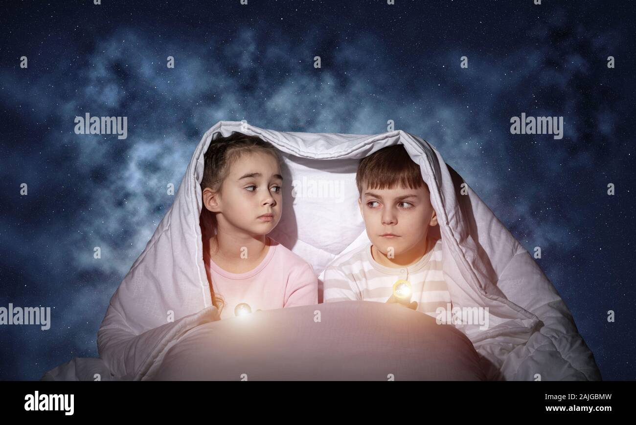 Children with flashlights lying in bed. Sister and brother hiding under ...