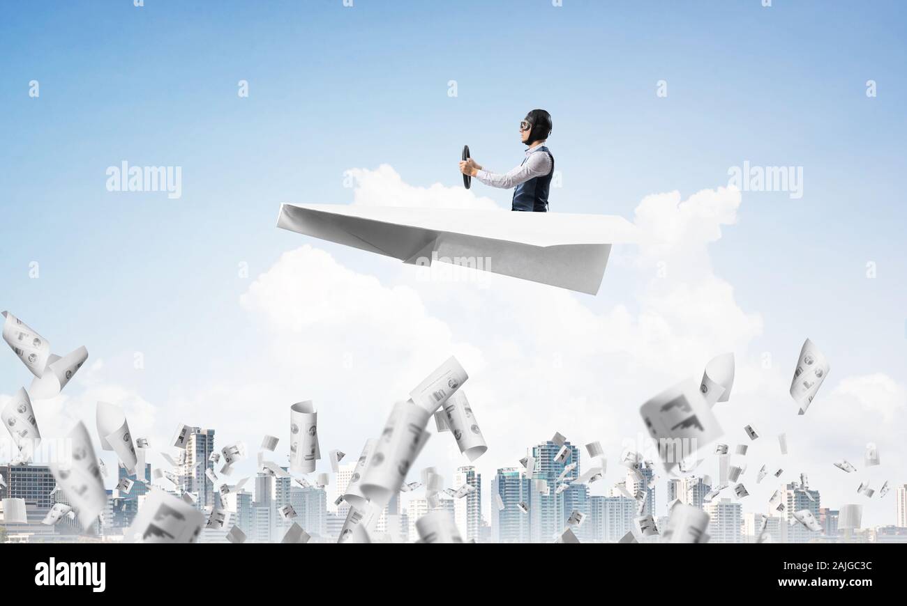 Aviator driving paper plane above business center in cloudy blue sky ...