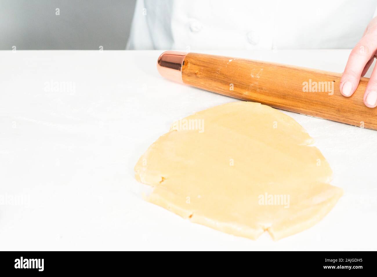 Rolling sugar cookie dought with wood rolling pin on a white table ...