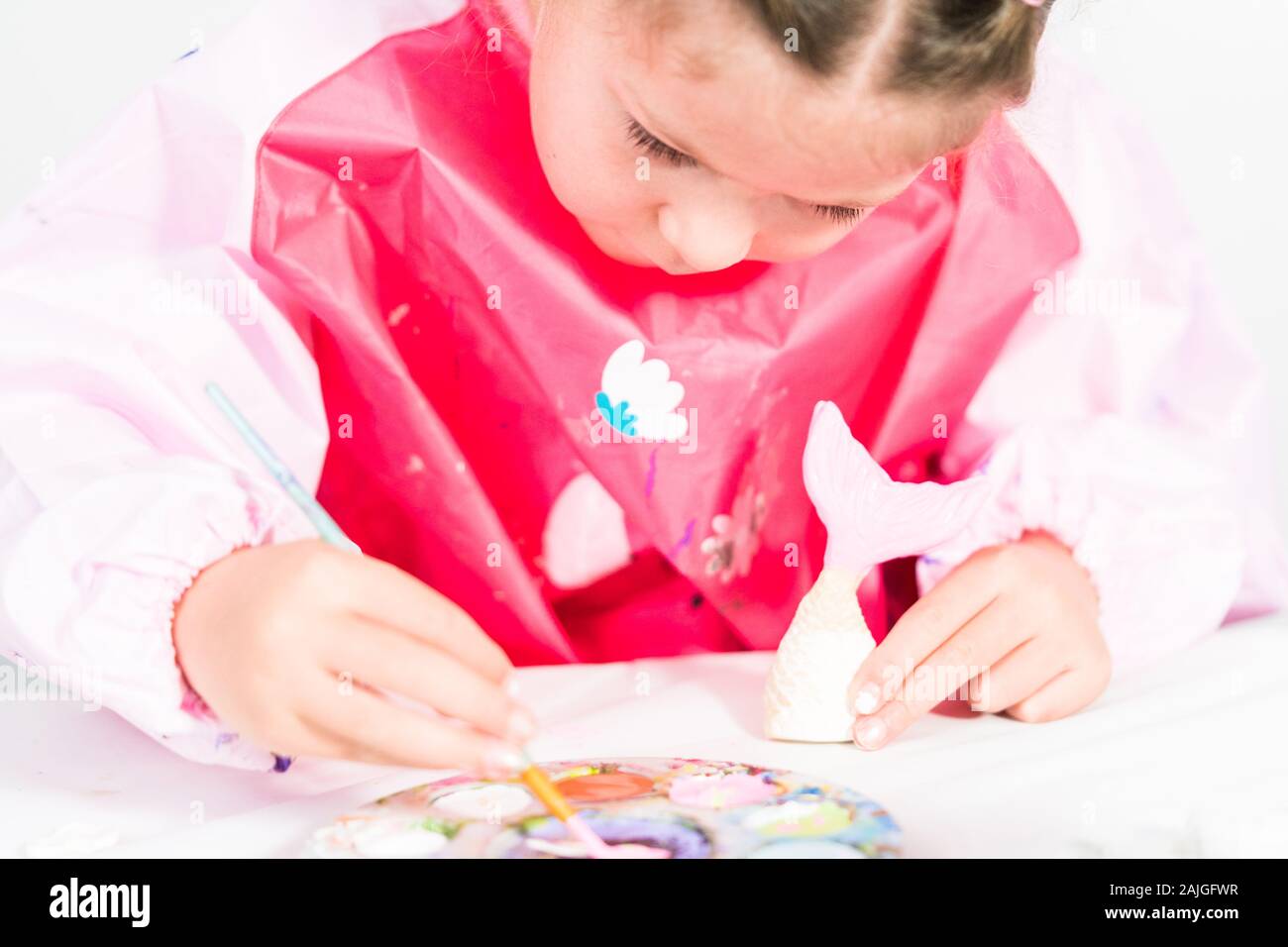 Little girl painting mermaid tails made out of modeling clay with ...