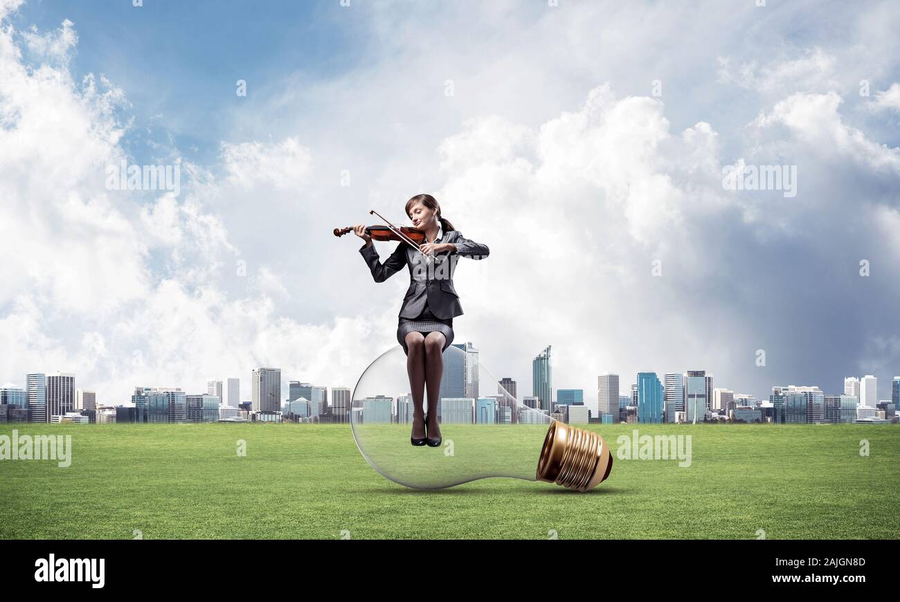 Young woman with violin sitting on big light bulb. Attractive ...