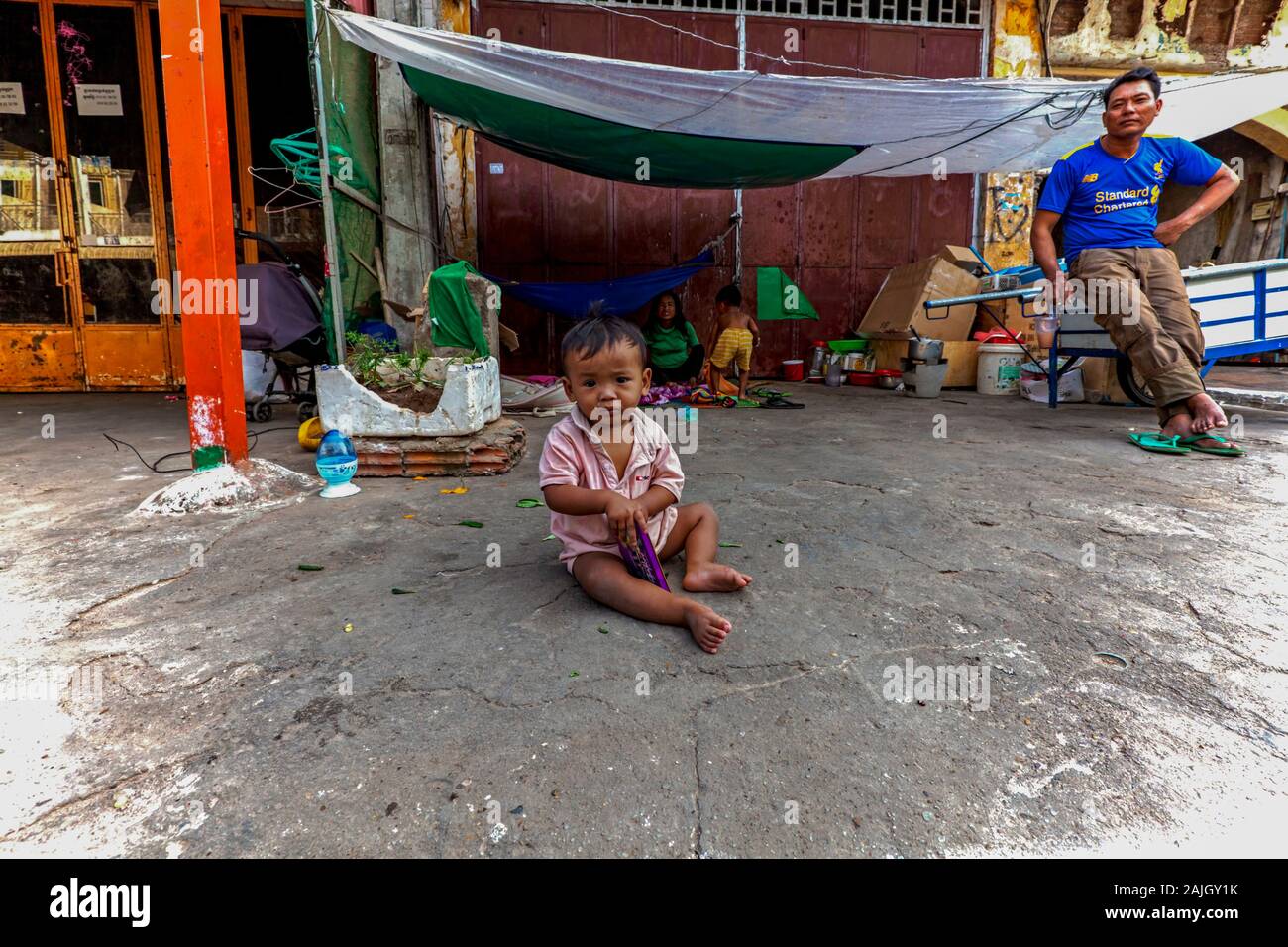 A poor young Asian boy toddler is sitting on a sidewalk in front of his ...