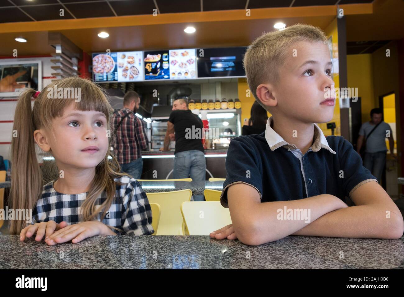 Children sitting in fast food restaurant behind empty table waiting for ...