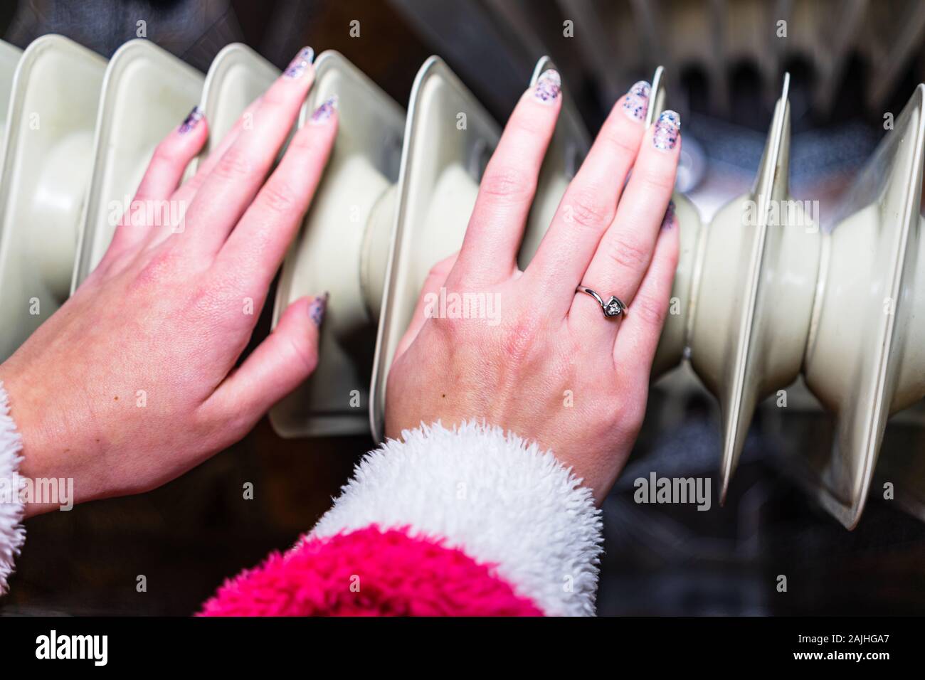 Close-up of a woman warming up her hands on a white radiator at home ...