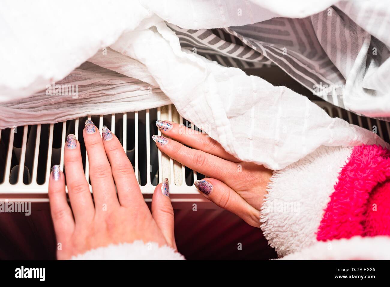 Close-up of a woman warming up her hands on a white radiator at home ...
