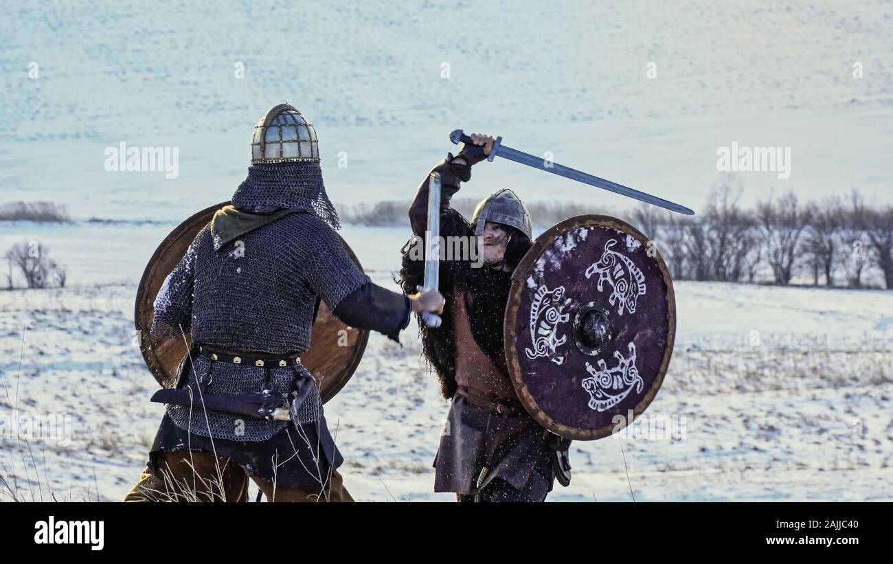 Two viking are fighting with axes and shields on the winter meadow ...