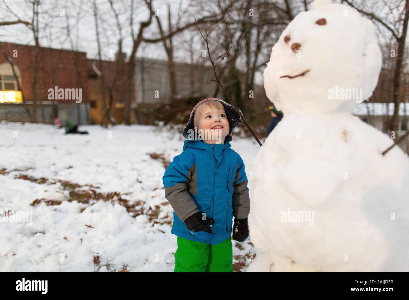 Toddler boy smiling while looking up at large snowman's face in winter ...