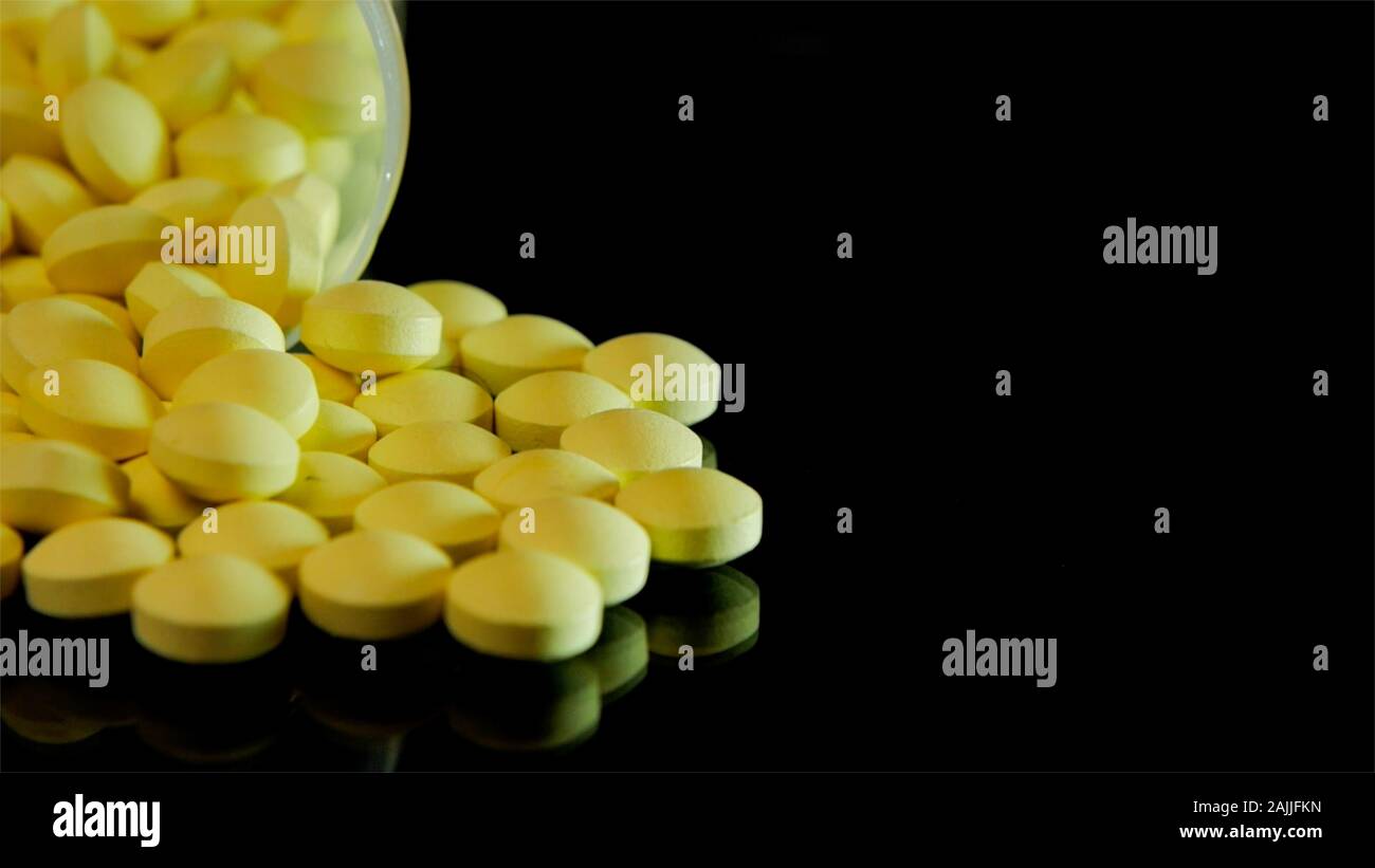 Yellow pills scattered from a transparent bottle are scattered on a ...