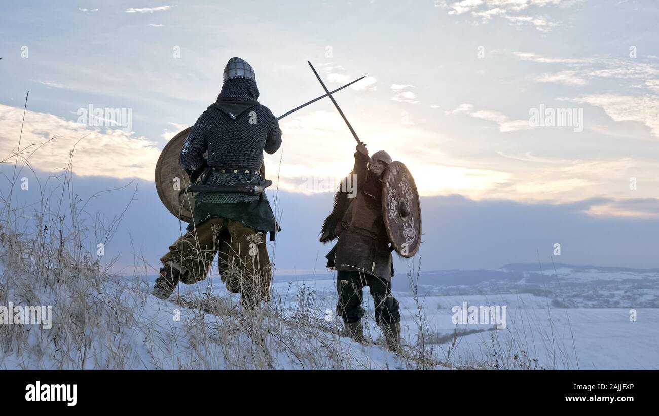 Two viking are fighting with axes and shields on the winter meadow ...